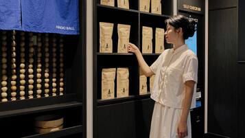 A woman in a white dress examining packaged items on shelves in a store with a blue cloth and wooden balls in the background.