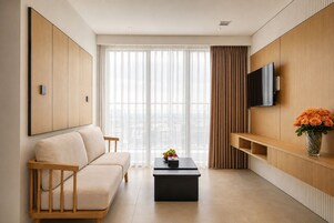 Uma sala de estar moderna com sofá, mesa de centro, televisão e vista através de grandes janelas.
