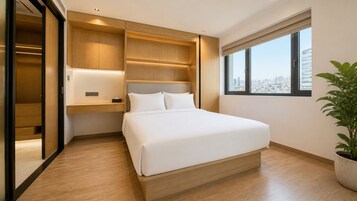 Quarto de hotel moderno com cama, estantes embutidas, uma janela grande com vista para a cidade e uma planta em vaso.