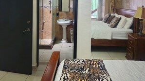 Quarto de hotel com cama, mesa de cabeceira, espelho, janela com cortinas e banheiro privativo com chuveiro, pia e vaso sanitário.