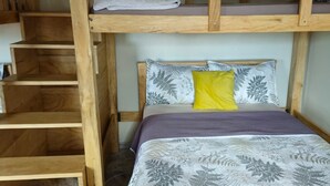 Uma cama de solteiro com escada de madeira, uma cama individual com colcha estampada e um travesseiro.