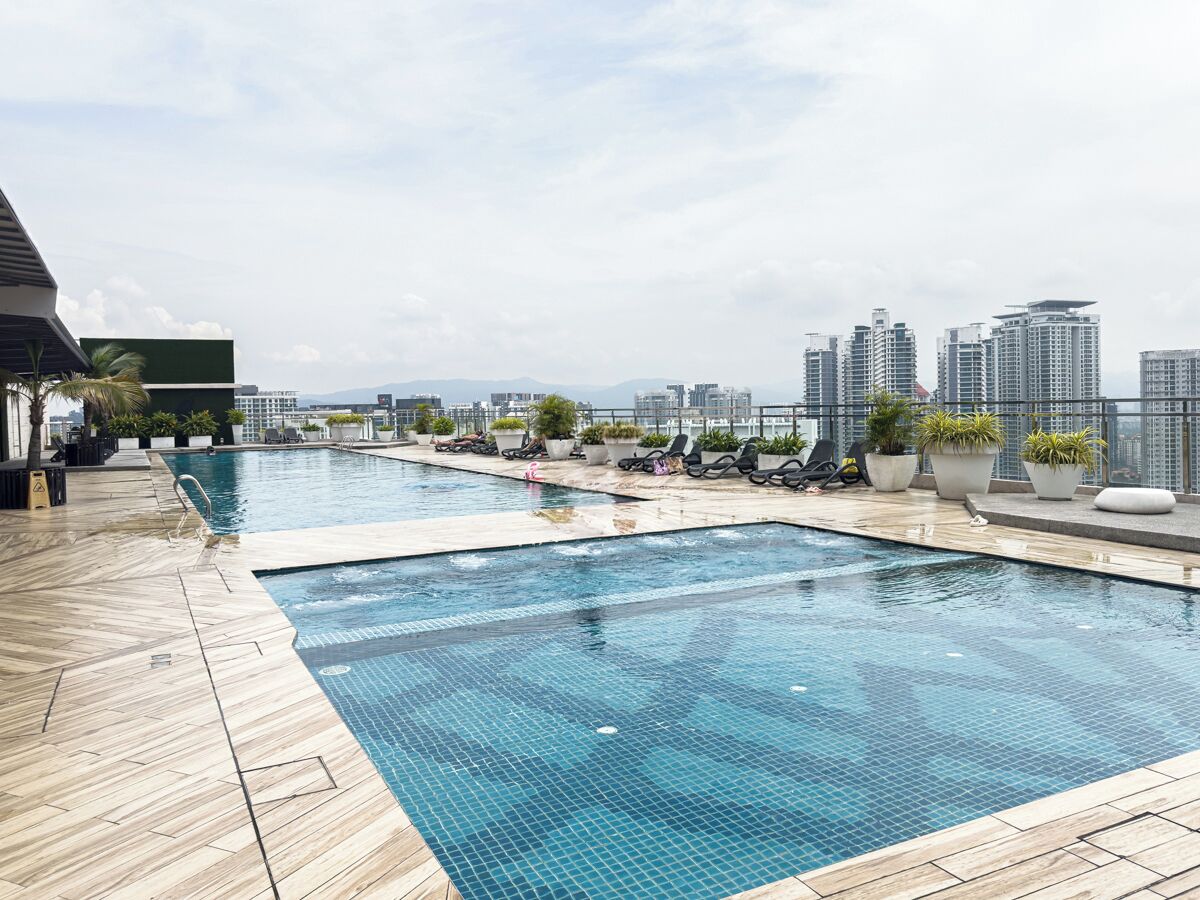 Piscina no terraço com espreguiçadeiras e plantas em vasos, cercada por edifícios altos.