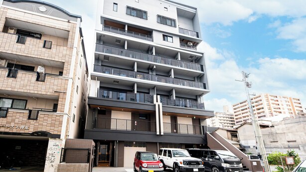 Um edifício residencial com vários andares, varandas, entrada de garagem e veículos estacionados.