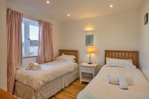Quarto de hotel com duas camas de solteiro, mesa de cabeceira com abajur, janela com cortinas e luminária na parede.