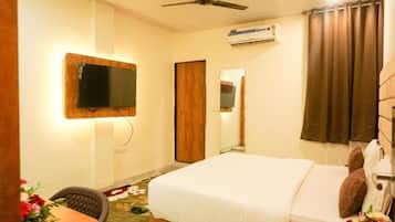 Quarto de hotel com cama, televisão fixada na parede, aparelho de ar condicionado e ventoinha de teto.