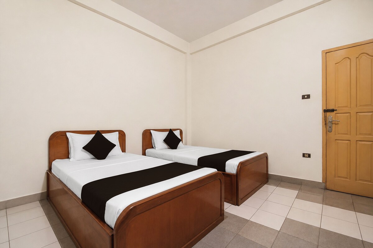 Quarto com duas camas de madeira, cada uma com colchão branco e almofadas decorativas pretas.