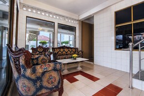 Um hall com sofás ornamentados, uma mesa de centro e vista através de grandes janelas.