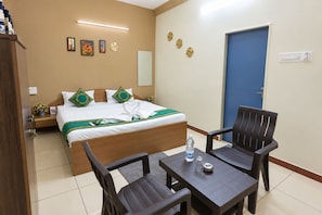 Quarto de hotel com cama, duas cadeiras, mesa, mesinha de cabeceira, relógio de parede, espelho, porta e parede decorada com pratos.