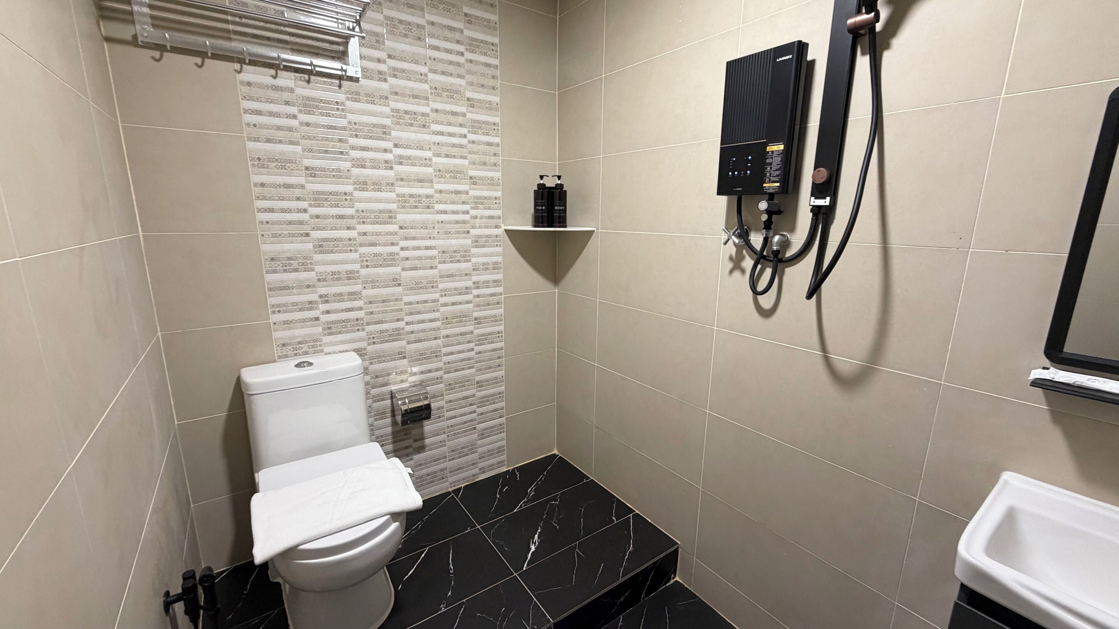 Casa de banho com sanita, cabine de duche e suporte para papel higiénico.