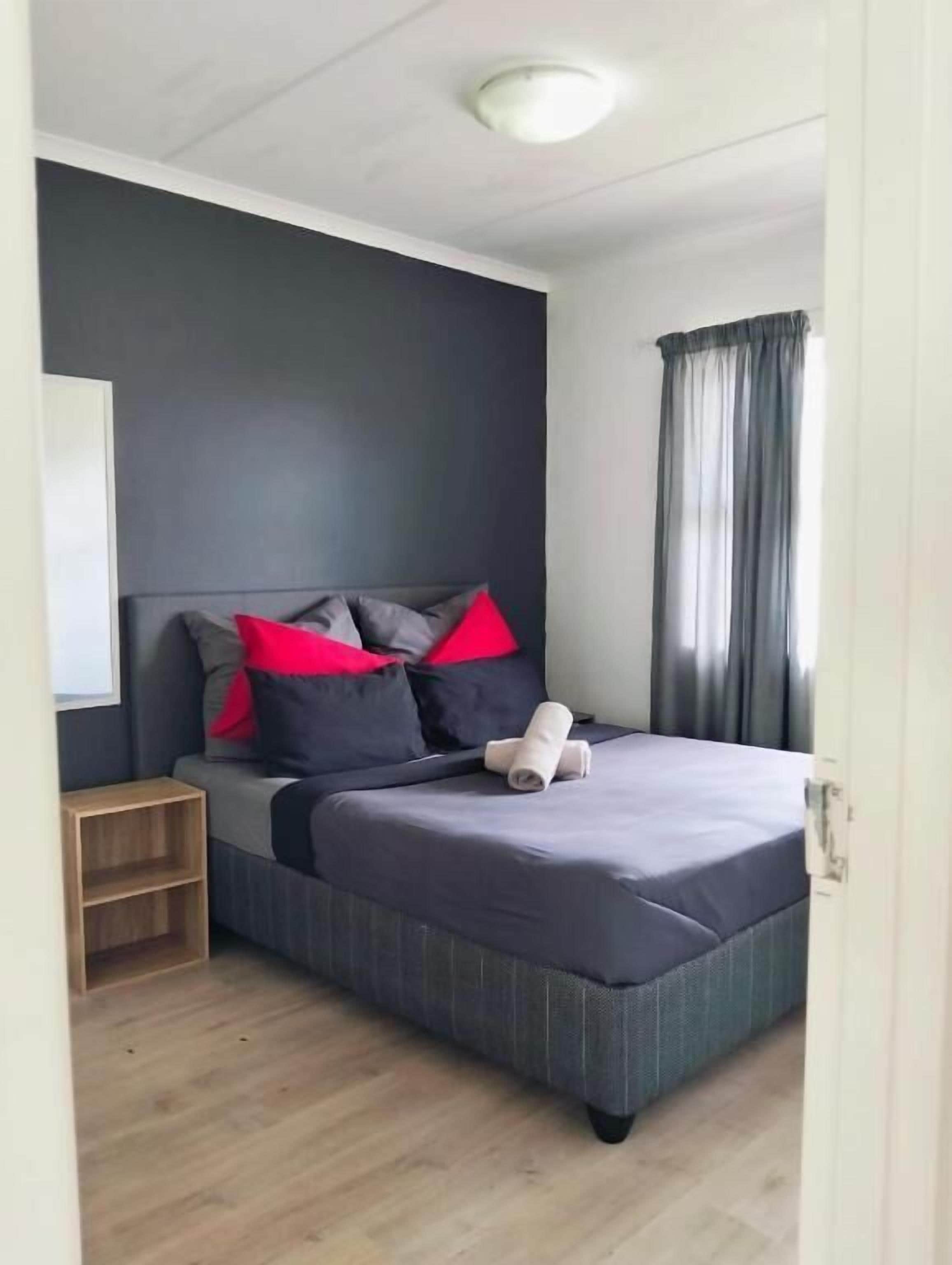 Quarto com cama, mesa de cabeceira e janela com cortinas.