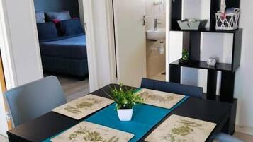 Uma área de refeições com uma mesa posta para quatro pessoas, uma planta em vaso e uma prateleira preta fixada na parede com diversos objetos.