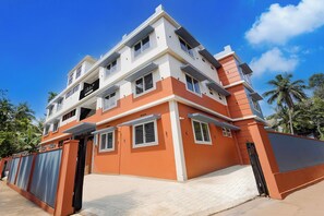 Um edifício residencial de vários andares com telhado plano, várias varandas e entrada com portão.