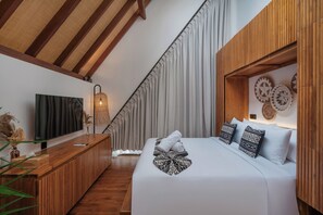 Um quarto moderno com teto de madeira, uma cama grande com almofadas estampadas, uma mesa de cabeceira com abajur e uma TV fixada na parede.