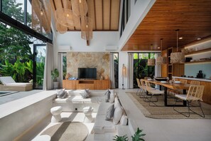 Uma sala de estar moderna com uma parede de pedra, uma televisão de tela plana e uma área de jantar com mesa e cadeiras de madeira.