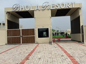 A entrada do Bhola Resort, com uma placa grande, portão e caminho pavimentado.