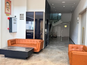 Um lobby moderno com assentos de couro, um quiosque de check-in e uma escada que dá acesso aos andares superiores.