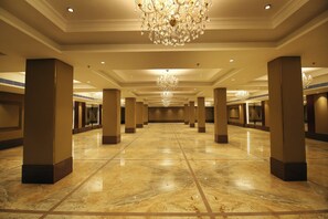 Um hall de hotel espaçoso com piso de mármore, grandes colunas e lustres elaborados.