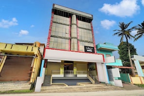 Um edifício com vários andares, entrada central, escadaria que dá acesso ao andar térreo e uma placa indicando serviço de recolha.