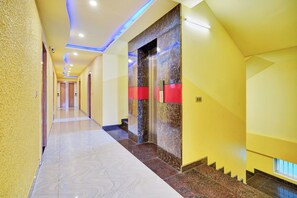 Corredor de hotel com piso de mármore, paredes amarelas e um elevador vermelho.