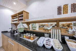 Uma área de buffet com diversos tipos de comida, copos e uma estação de café.