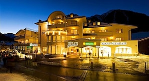 Um hotel com vários andares e varandas, uma entrada visível e lojas adjacentes.