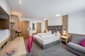 Quarto de hotel moderno com uma cama grande, mesas de cabeceira, escrivaninha e um sofá.