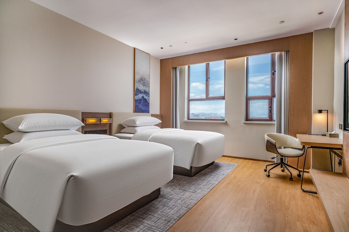 Quarto de hotel moderno com duas camas, uma escrivaninha e uma cadeira.
