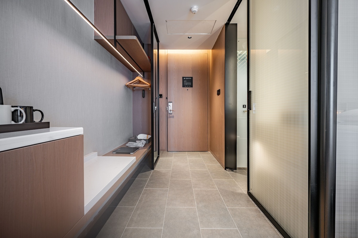 Corredor moderno de hotel com balcão de recepção, porta-casacos e porta de elevador de vidro.