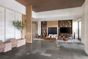 Uma sala de estar moderna com televisão de tela plana, um sofá e uma mesa de centro. Há uma estante com objetos decorativos e um vaso de planta.