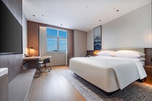 Quarto de hotel moderno com uma cama grande, uma escrivaninha e uma janela vista para a cidade.