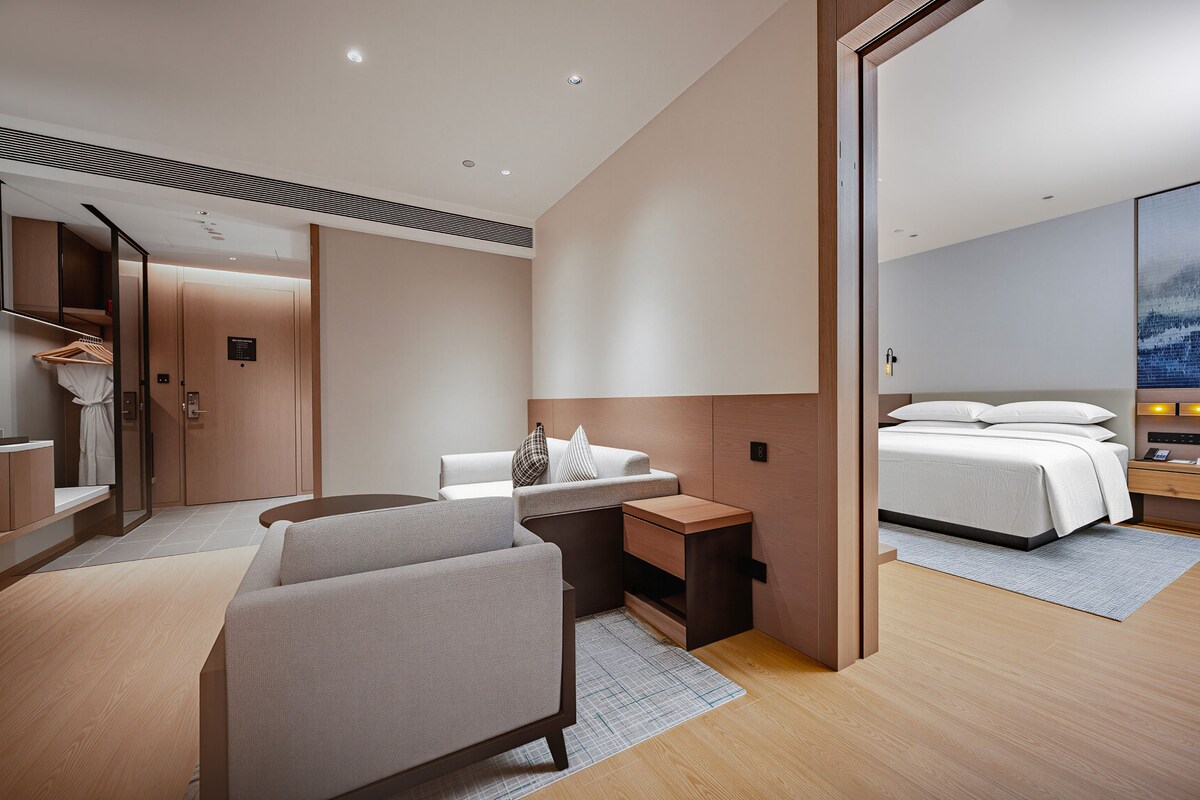 Quarto de hotel moderno com sofá, mesa pequena, cama e banheiro com chuveiro e vaso sanitário.