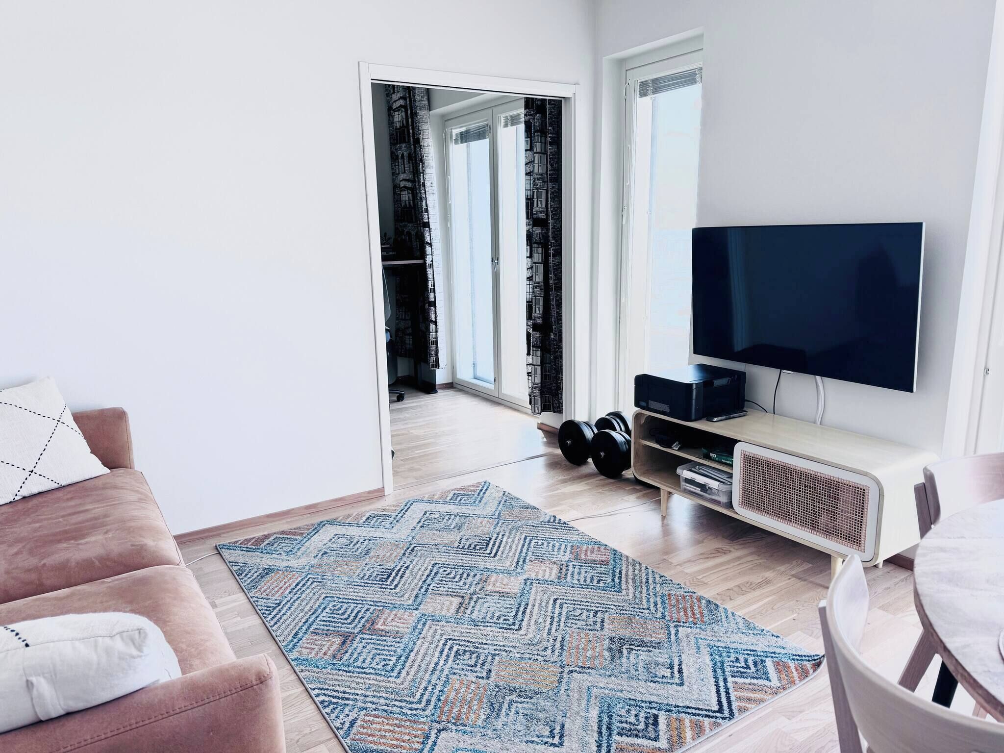Uma sala de estar moderna com uma televisão de tela plana, uma mesa de centro, um sofá e um tapete estampado.