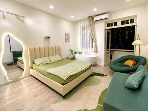 Quarto moderno com cama, área de estar com poltrona, janela com cortinas e aparelho de ar condicionado.
