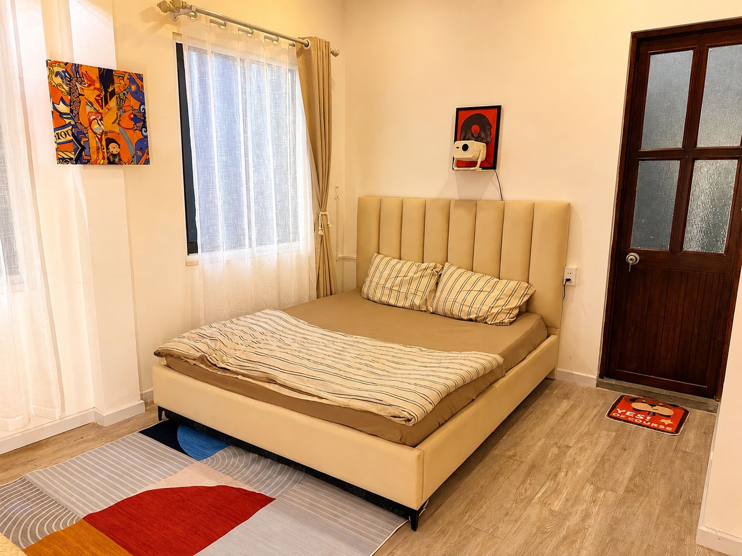 Quarto com cama, cortinas, uma porta e um quadro pendurado na parede.