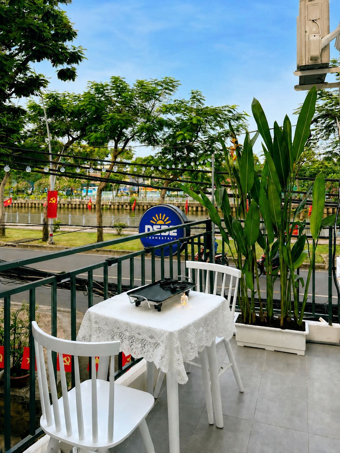 Terraço com mesa e cadeiras, corrimão e vista para um rio com bandeiras.