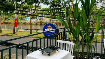 Terraço com mesa e cadeiras, corrimão e vista para um rio com bandeiras.