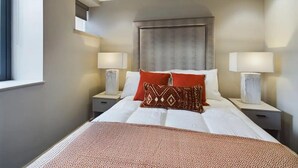Quarto de hotel com uma cama, duas mesas de cabeceira, uma janela e uma luminária no teto.