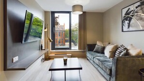A modern living room with a sofa, a coffee table, and a large window offering a view of buildings and trees.