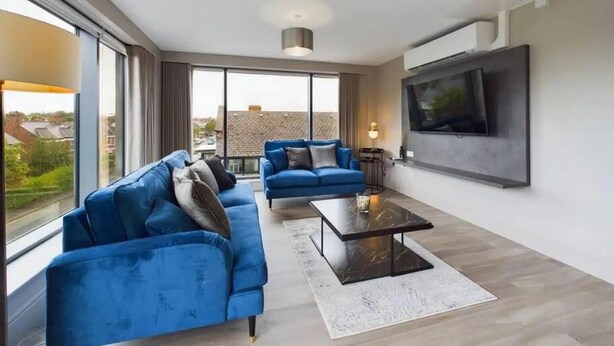 A modern living room with a sectional sofa, a coffee table, and a flat-screen TV mounted on the wall.
