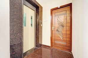Um corredor com piso de mármore, porta de madeira com detalhes decorativos e parede em tons claros.