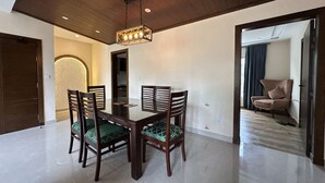 Uma sala de jantar com mesa e cadeiras de madeira, um lustre e vista para outro ambiente com uma poltrona.