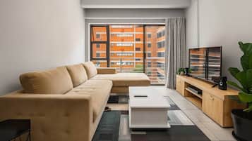 Uma sala de estar moderna com sofá, mesa de centro, televisão e vista para um prédio de tijolos.