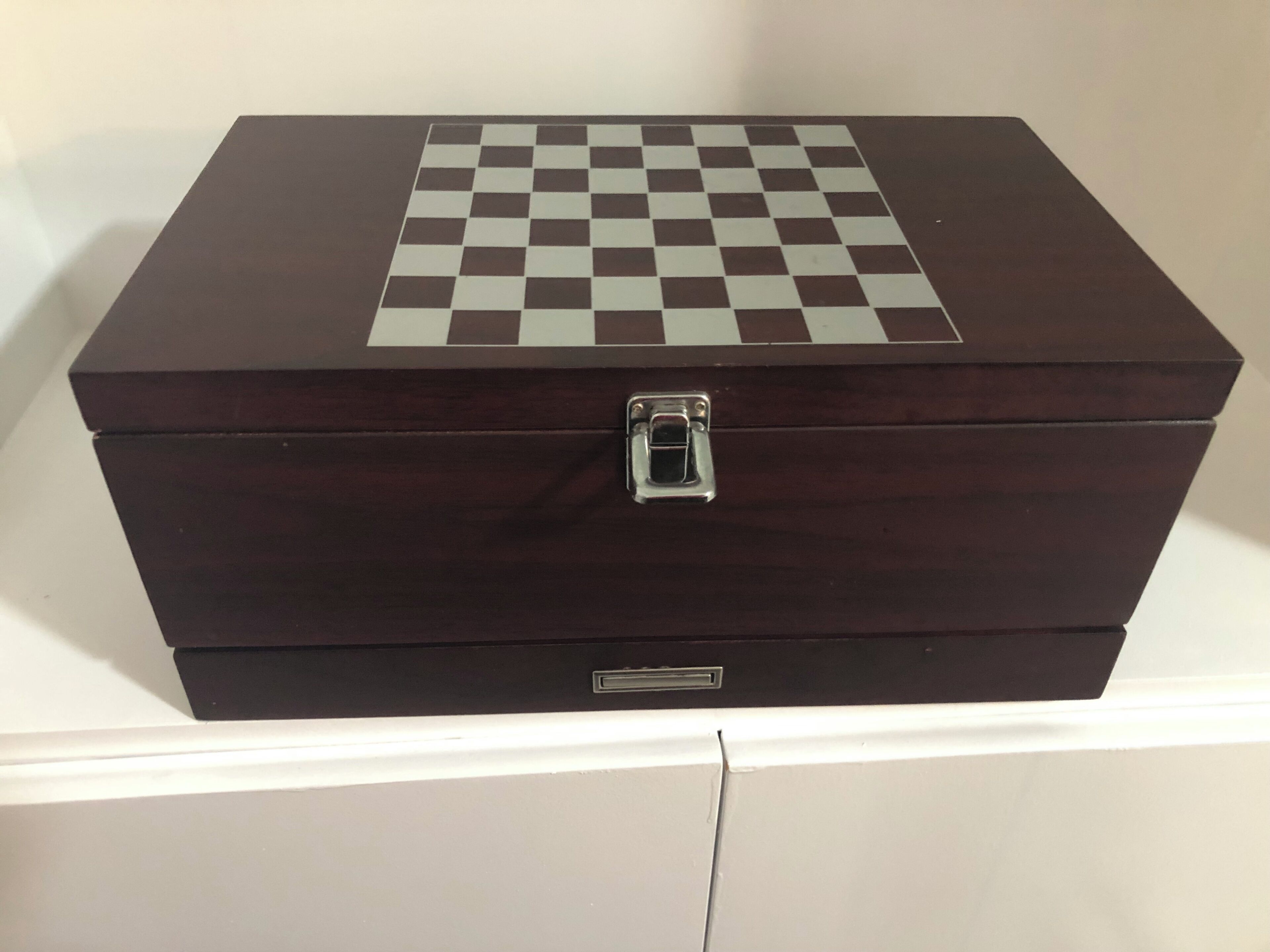 Uma caixa de madeira escura com padrão quadriculado na parte superior, uma trava de metal e uma pequena placa retangular na frente.