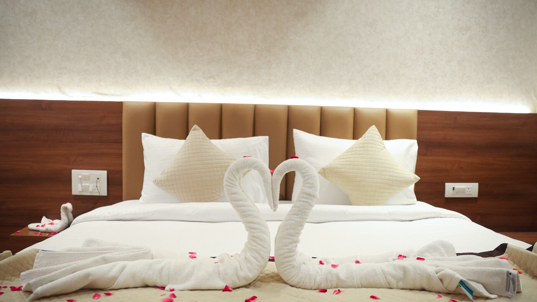 Quarto de hotel com uma cama grande, duas almofadas e toalhas dispostas em formato de coração.