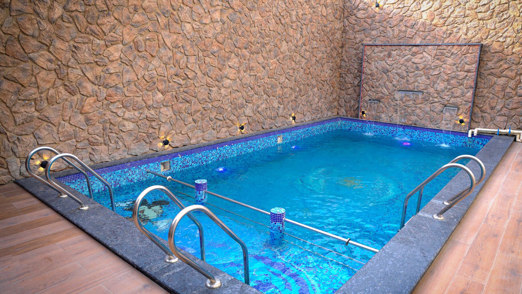Uma piscina interior retangular com um painel de parede de pedra, rodeada por um deck ladrilhado.