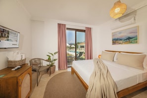 Quarto de hotel com cama, escrivaninha com computador, cadeira, planta e um quadro na parede.