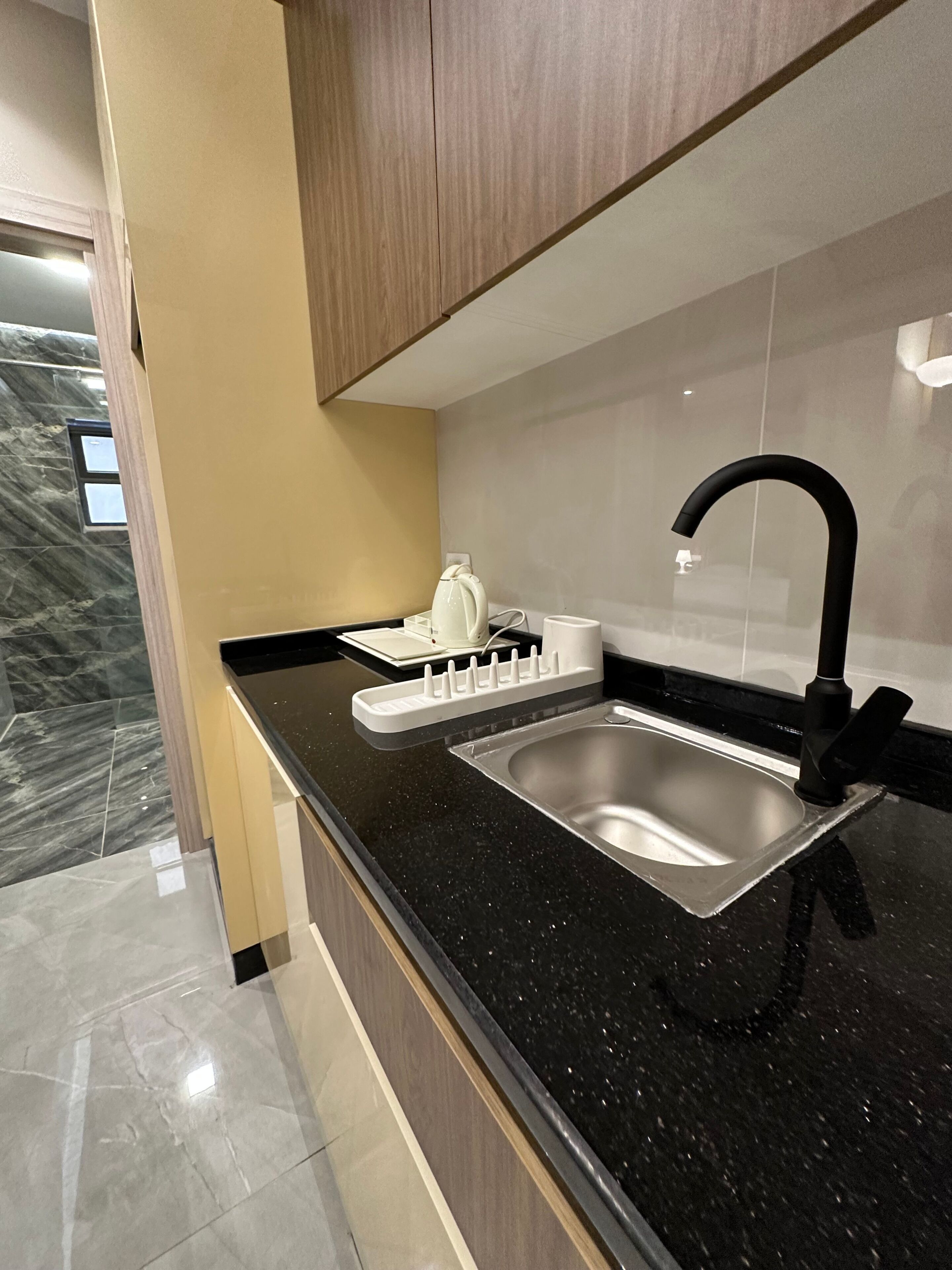 Uma cozinha moderna com bancada preta, pia de aço inoxidável e chaleira.