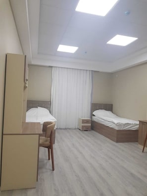 Quarto de hotel com duas camas, uma escrivaninha, uma cadeira e um guarda-roupa.