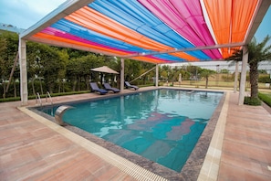 Uma piscina com toldo colorido, cadeiras de lounge e um deck revestido com azulejos.