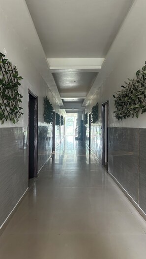Um corredor comprido e estreito com piso brilhante, portas em ambos os lados e plantas verdes nas paredes.